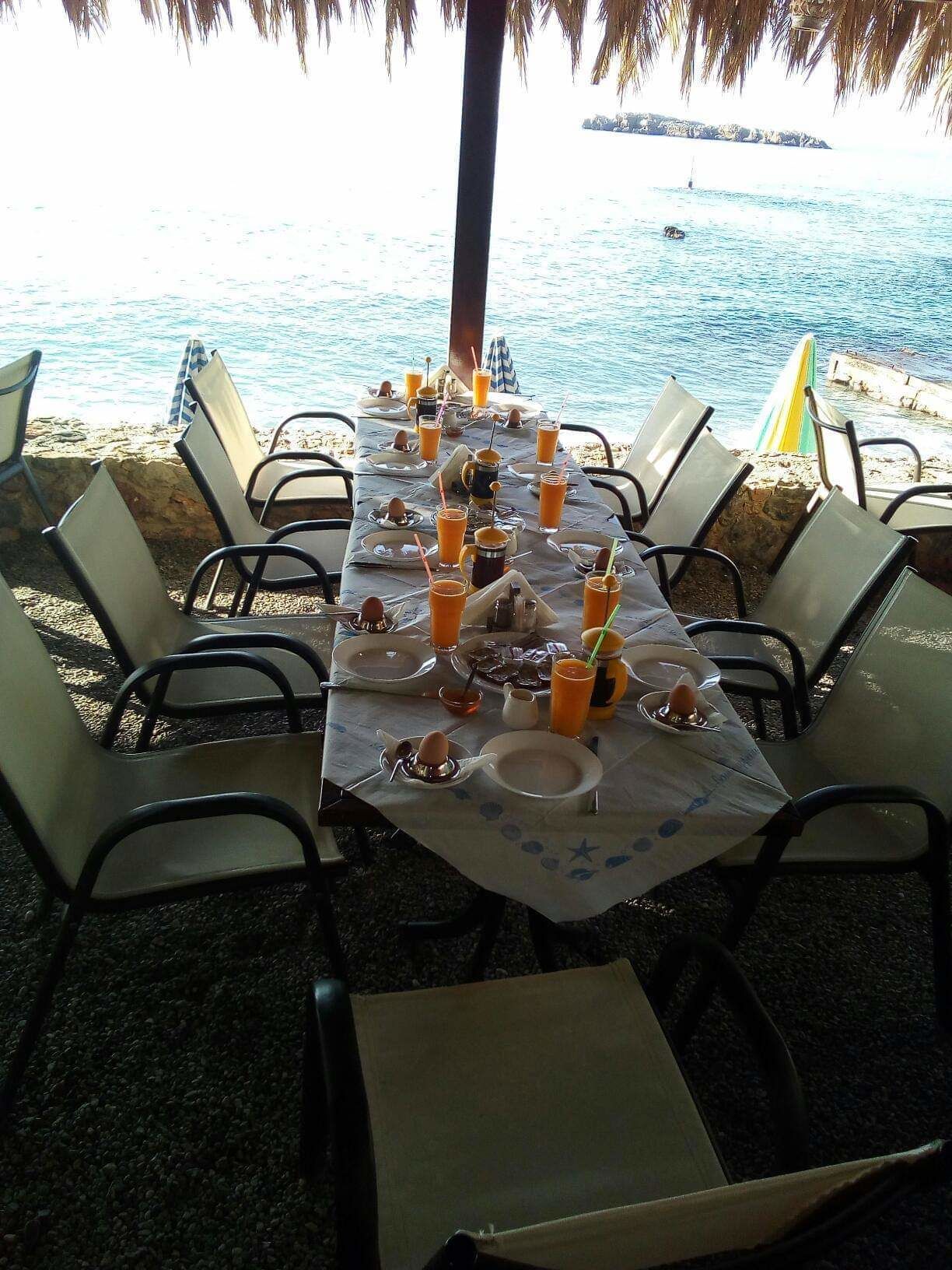 Mesa posta para refeição com cadeiras, com vista para a praia e para o mar.