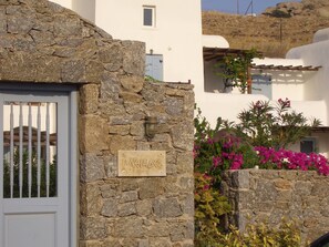 Um muro de pedra com uma placa indicando "DAGIANES" e uma porta branca com barras verticais.