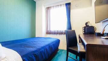 Quarto de hotel com cama, escrivaninha, cadeira, televisão e janela com cortinas.