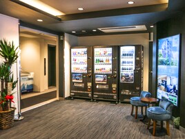 Um saguão de hotel com máquinas de venda automática, área de estar e balcão de recepção.