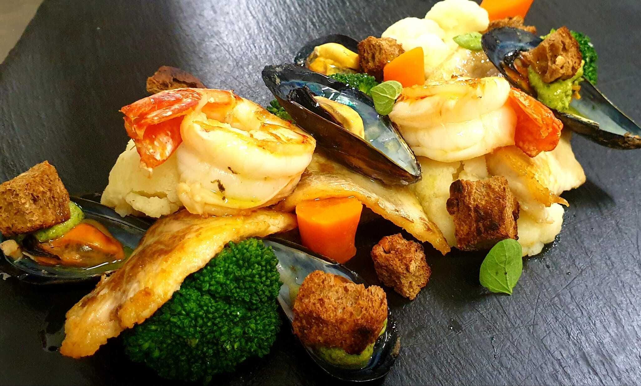 Prato de frutos do mar com mexilhões, camarões e legumes em um prato de ardósia.