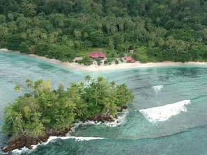 Vista aérea de uma ilha tropical com águas turquesa cristalinas, uma pequena praia e vegetação densa.