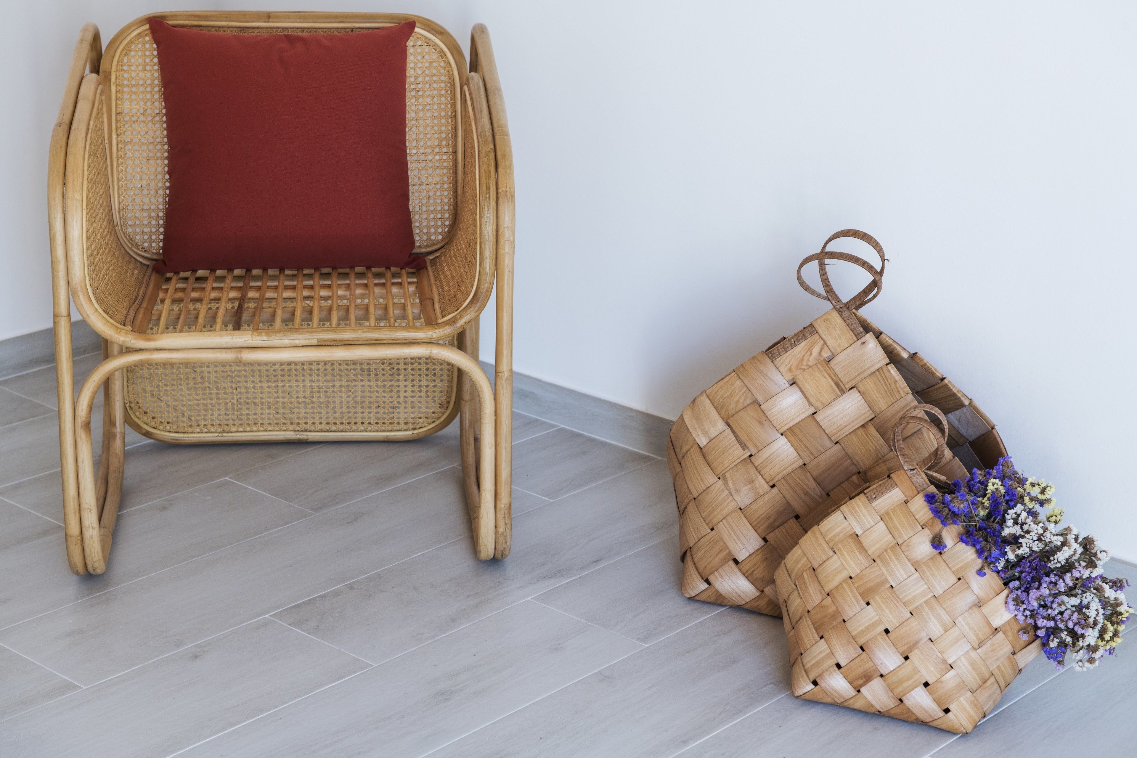 Uma cadeira de vime com almofada vermelha e uma bolsa tecida com flores sobre um chão de azulejos.