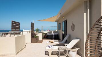 Terraço no telhado com cadeiras de lounge, ofurô e vista para o oceano.