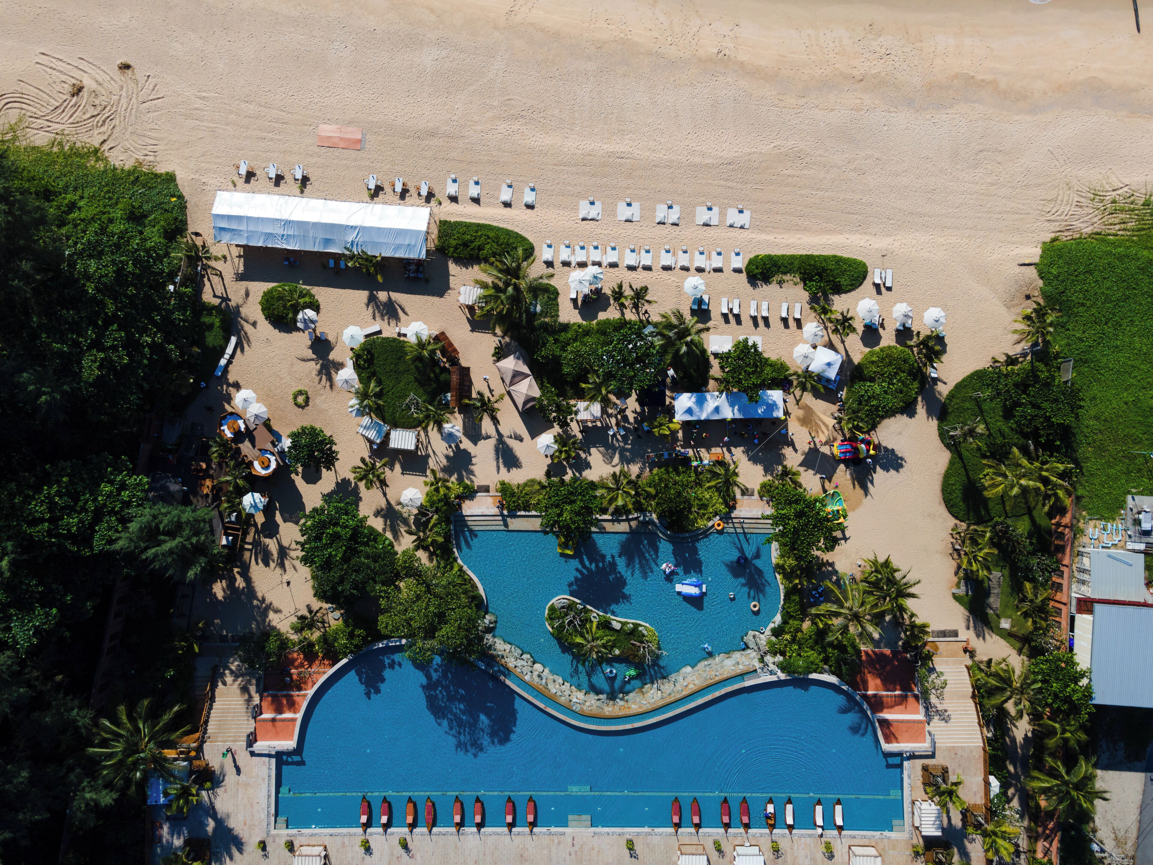 Vista aérea de um resort com piscina, espreguiçadeiras e palmeiras.