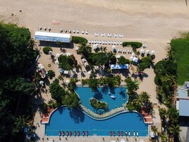 Vista aérea de um resort com piscina, espreguiçadeiras e palmeiras.