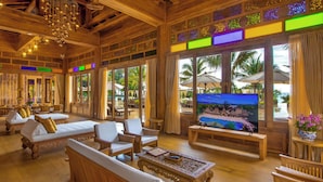 Quarto espaçoso com móveis de madeira, televisão e grandes janelas com vista para a praia.