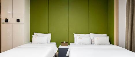 Quarto de hotel com duas camas, parede verde decorativa, minibar e guarda-roupa.