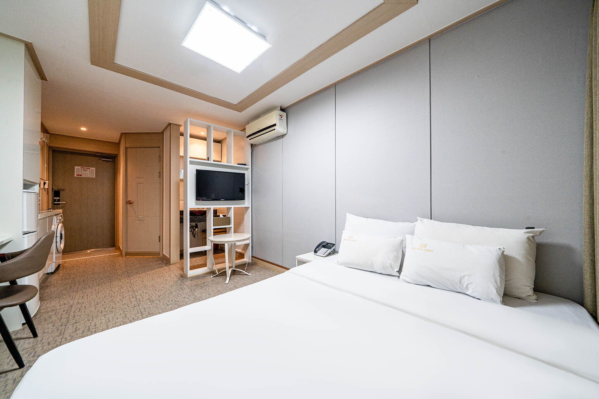 Quarto de hotel com cama, escrivaninha, cadeira, televisão e ar condicionado.