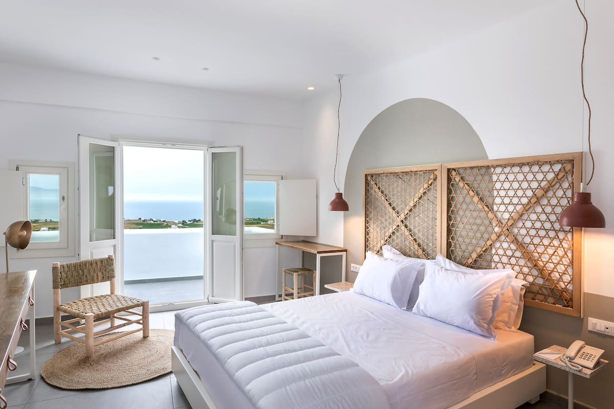 Quarto com cama, escrivaninha, cadeira e vista para o mar.