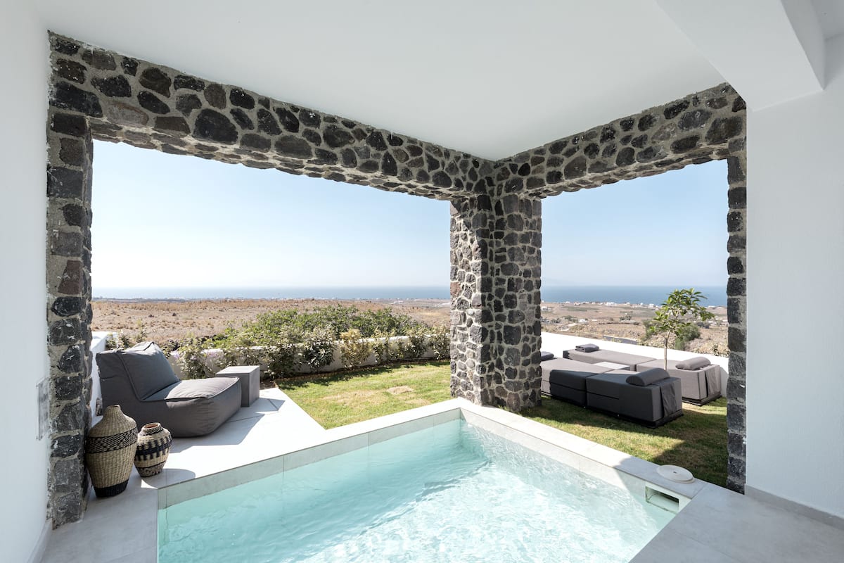Uma área de piscina com pilares de pedra, vista para o mar e mobiliário de exterior.