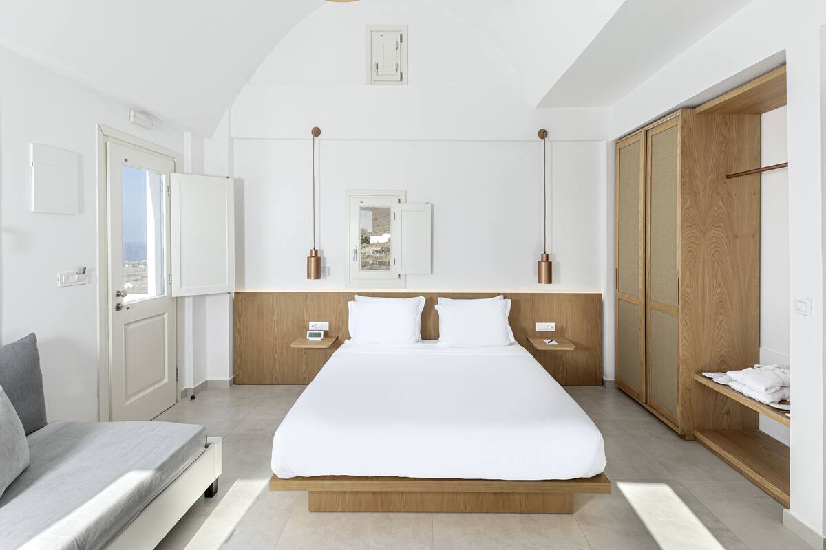 Quarto moderno com cama grande, mesas de cabeceira, guarda-roupa e vista para o exterior.