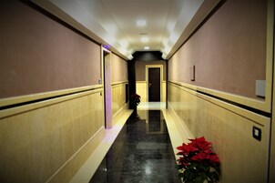 Um corredor com piso de mármore, uma porta no final e um vaso com flores vermelhas.