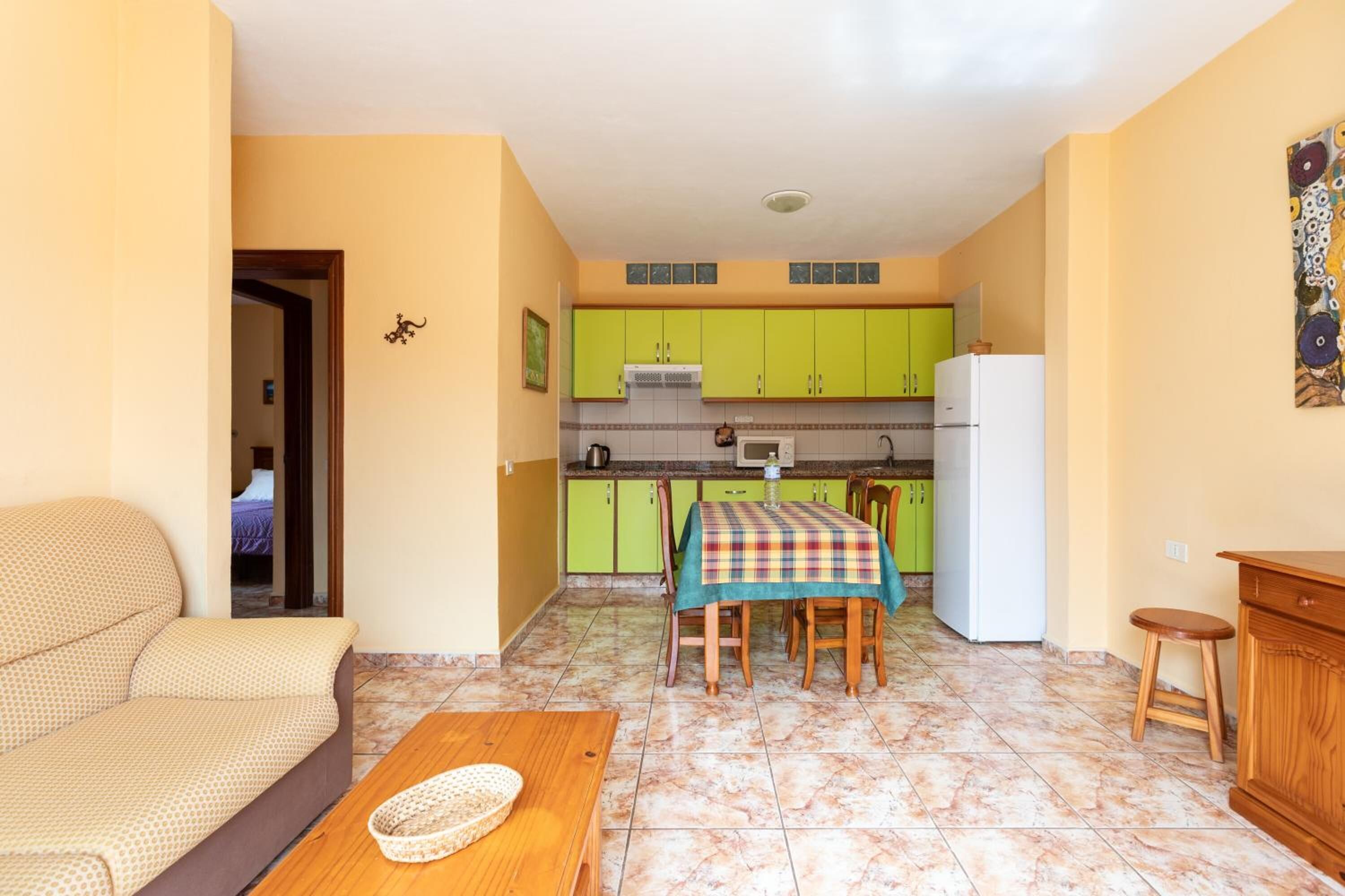 Um espaço de estar compacto com sofá, mesa de jantar com cadeiras, área de cozinha com armários verdes, geladeira branca e um armário de madeira.