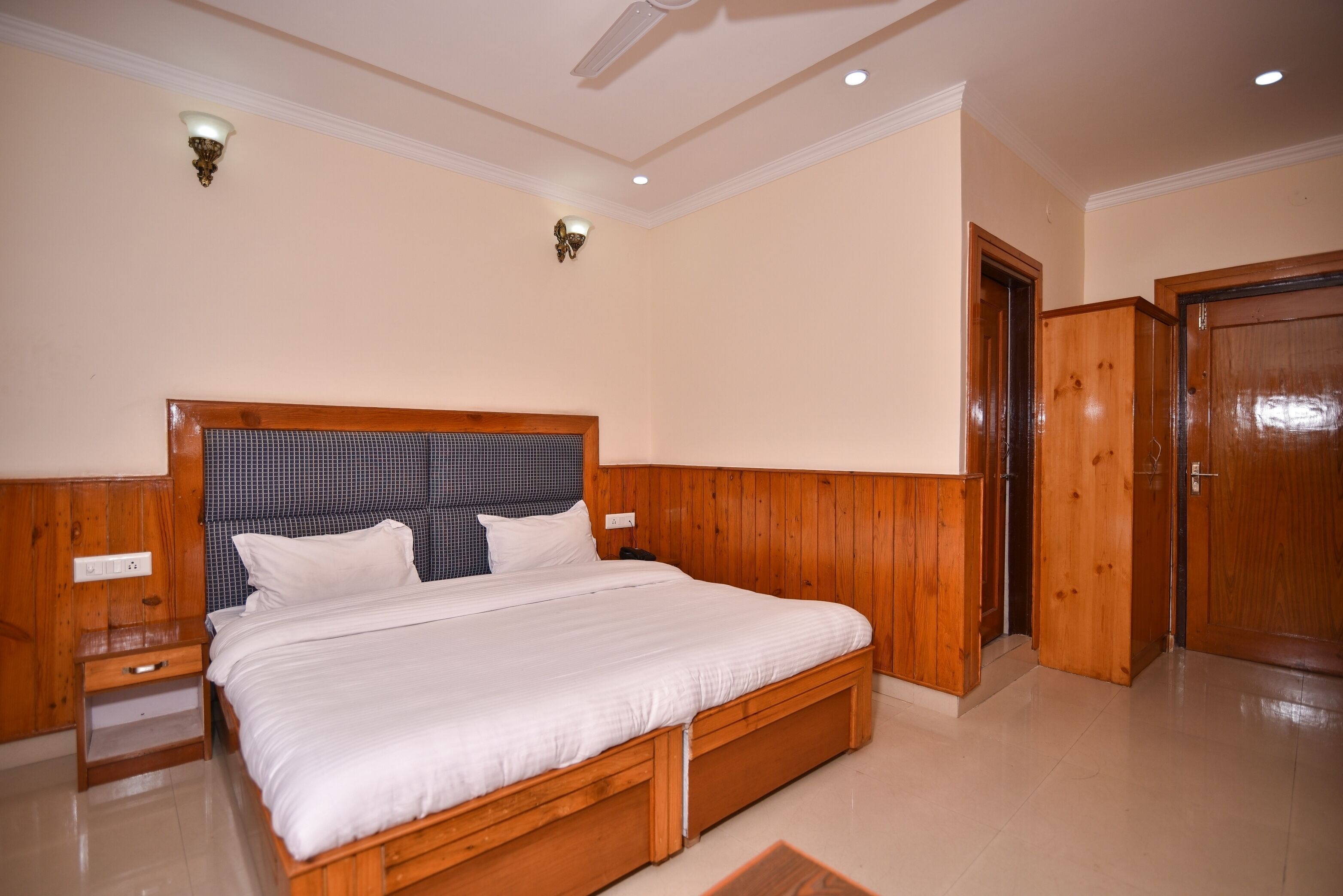Quarto com cama de madeira, mesa de cabeceira, guarda-roupa e ventoinha no teto.