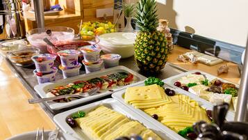 Buffet com diversas opções de comida, incluindo frutas, queijos e saladas.