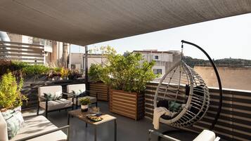 Terraço no telhado com área de estar externa, cadeira suspensa e vasos com plantas.