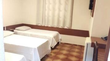 Quarto com duas camas de solteiro, piso de madeira, janela com cortinas e uma pequena mesa com uma cadeira.