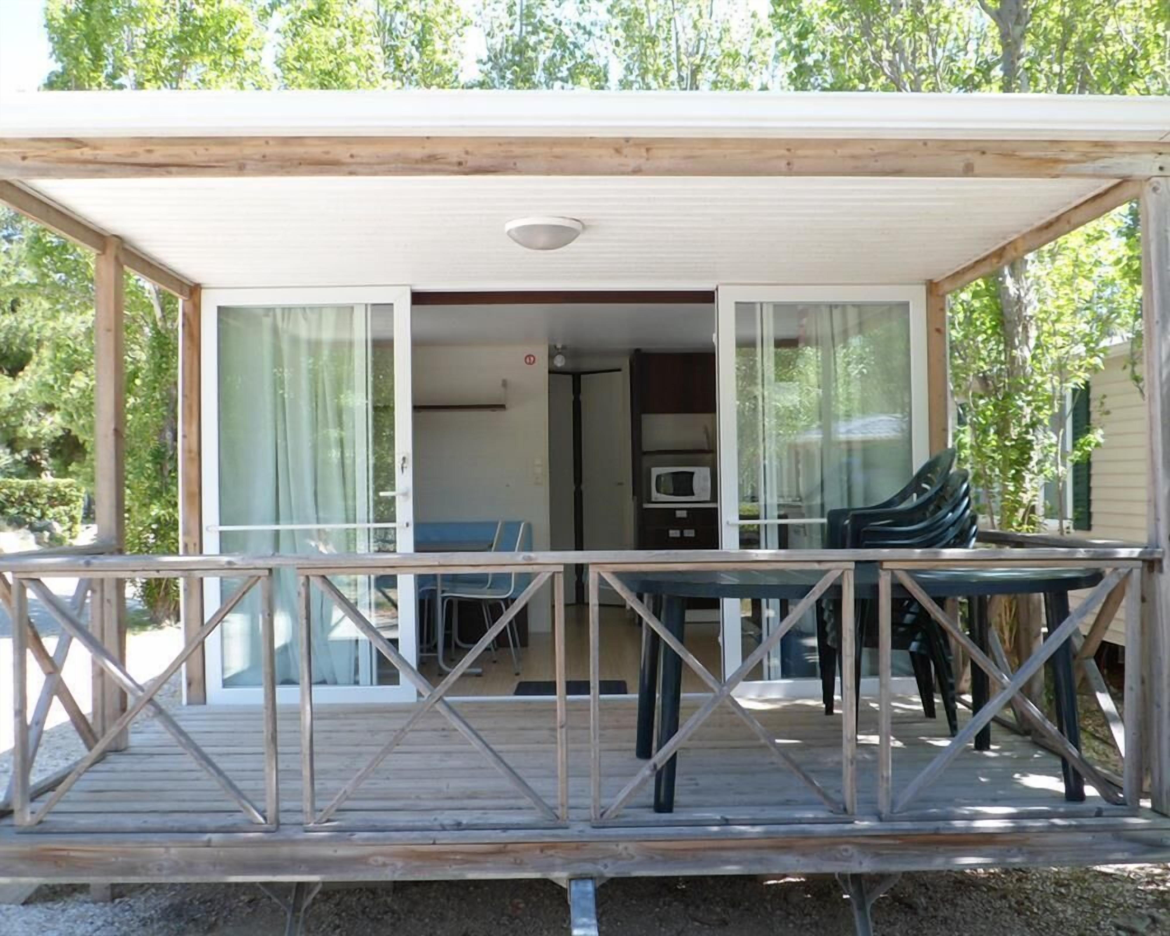 Um deck de madeira com uma porta de vidro que dá para um quarto com micro-ondas e uma cadeira azul.