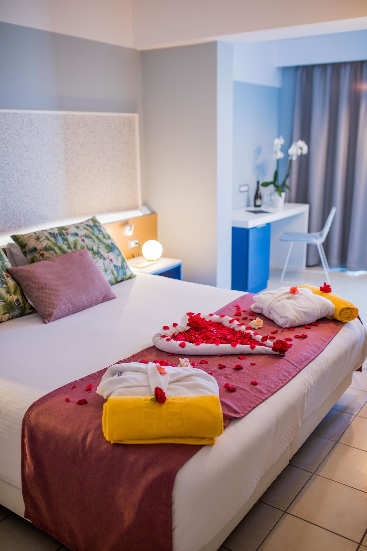 Quarto de hotel com cama, escrivaninha, cadeira e janela com cortinas.