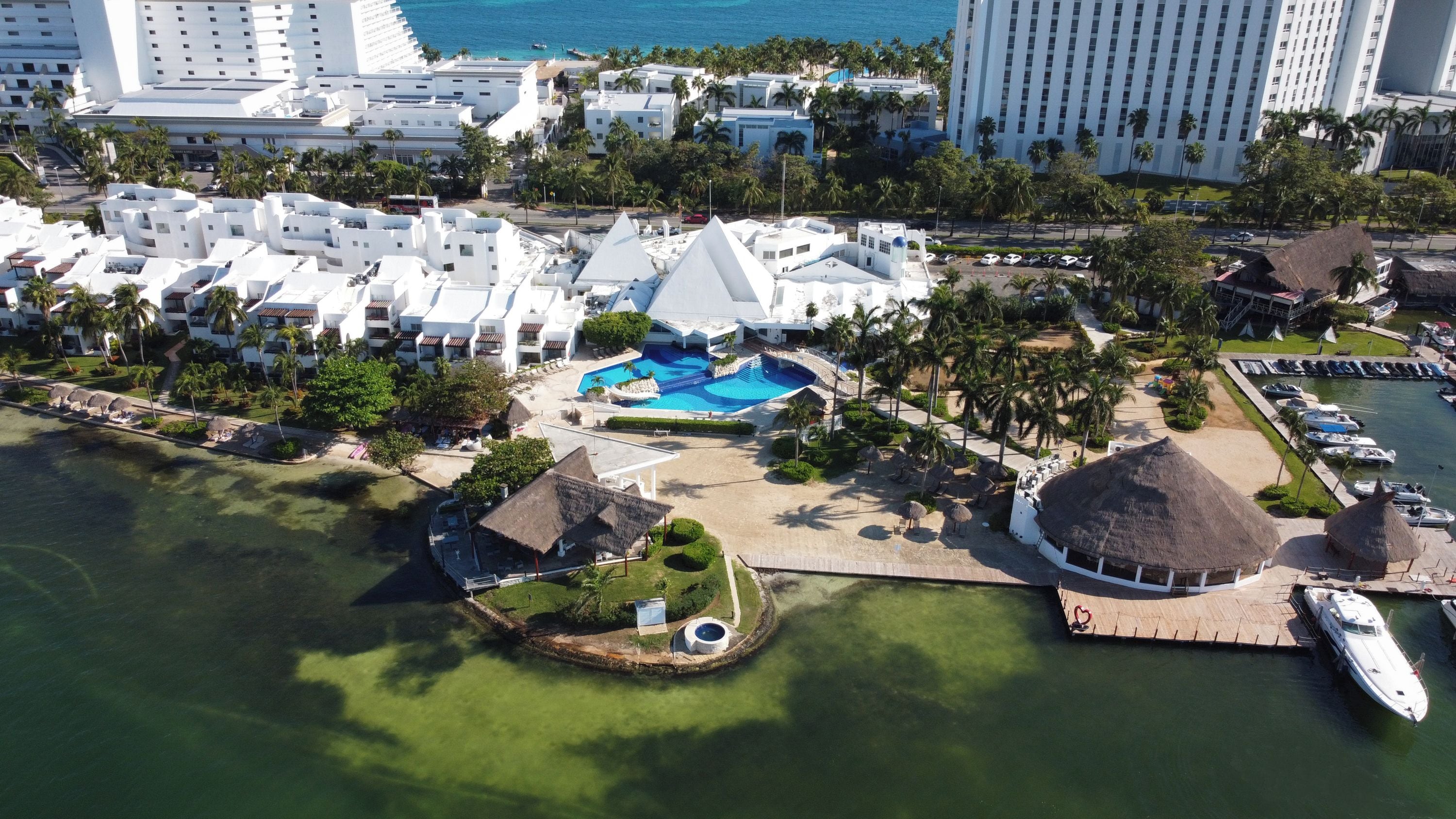 Vista aérea de um resort com piscina central, vários edifícios e um porto de iates.