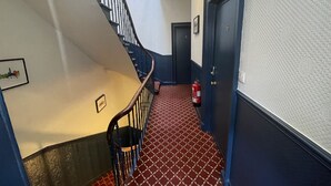 Um corredor com carpete vermelho estampado, guarda-corpo de metal preto e um extintor fixado na parede.