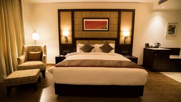 Quarto de hotel com uma cama grande, duas luminárias de cabeceira, uma cadeira e uma escrivaninha com chaleira.