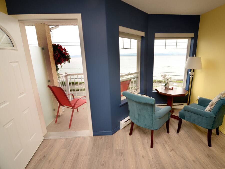 Quarto com vista para o mar, com duas cadeiras, uma mesa e um abajur.