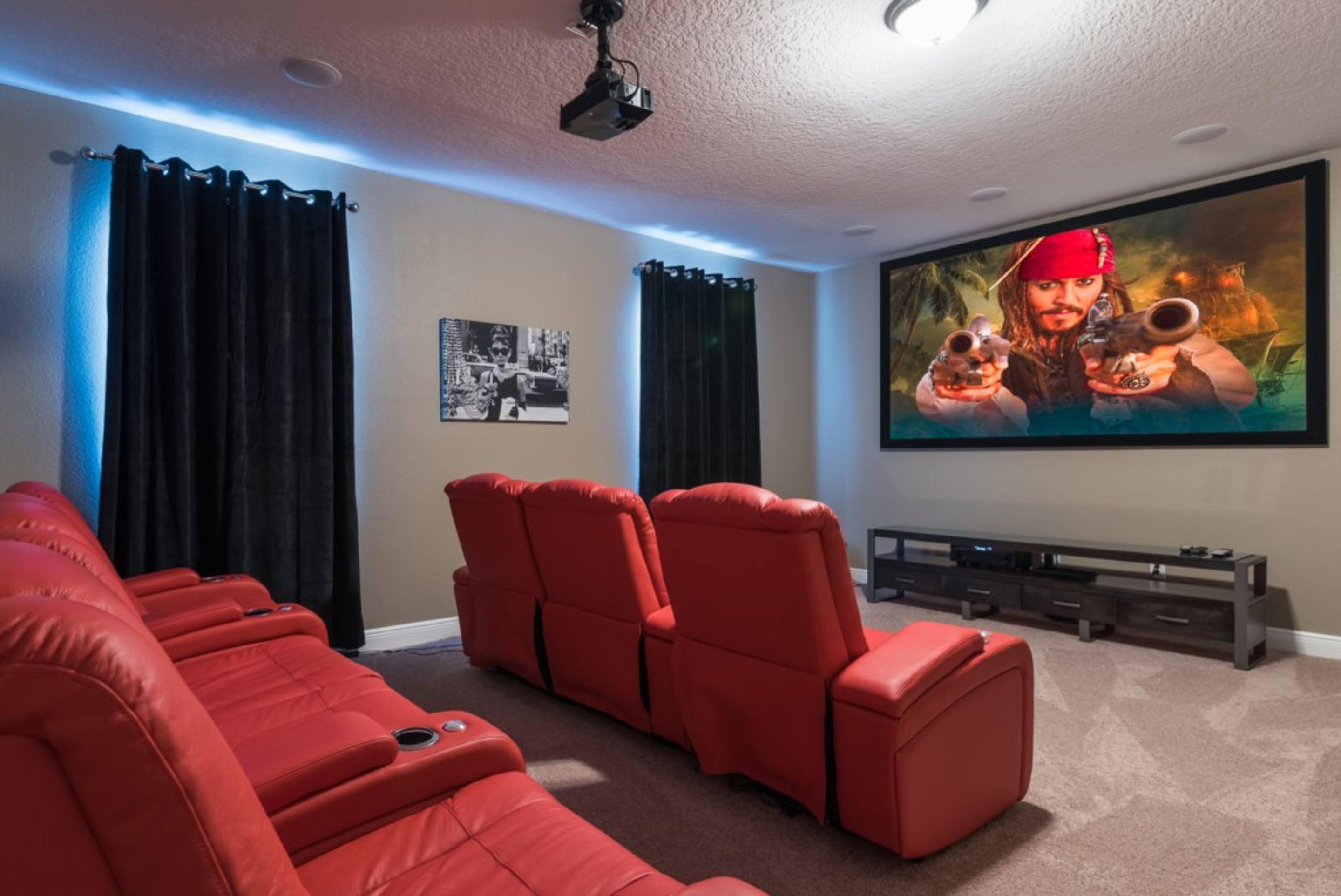 Uma sala de cinema com poltronas reclináveis vermelhas, uma TV de tela plana grande e um projetor.