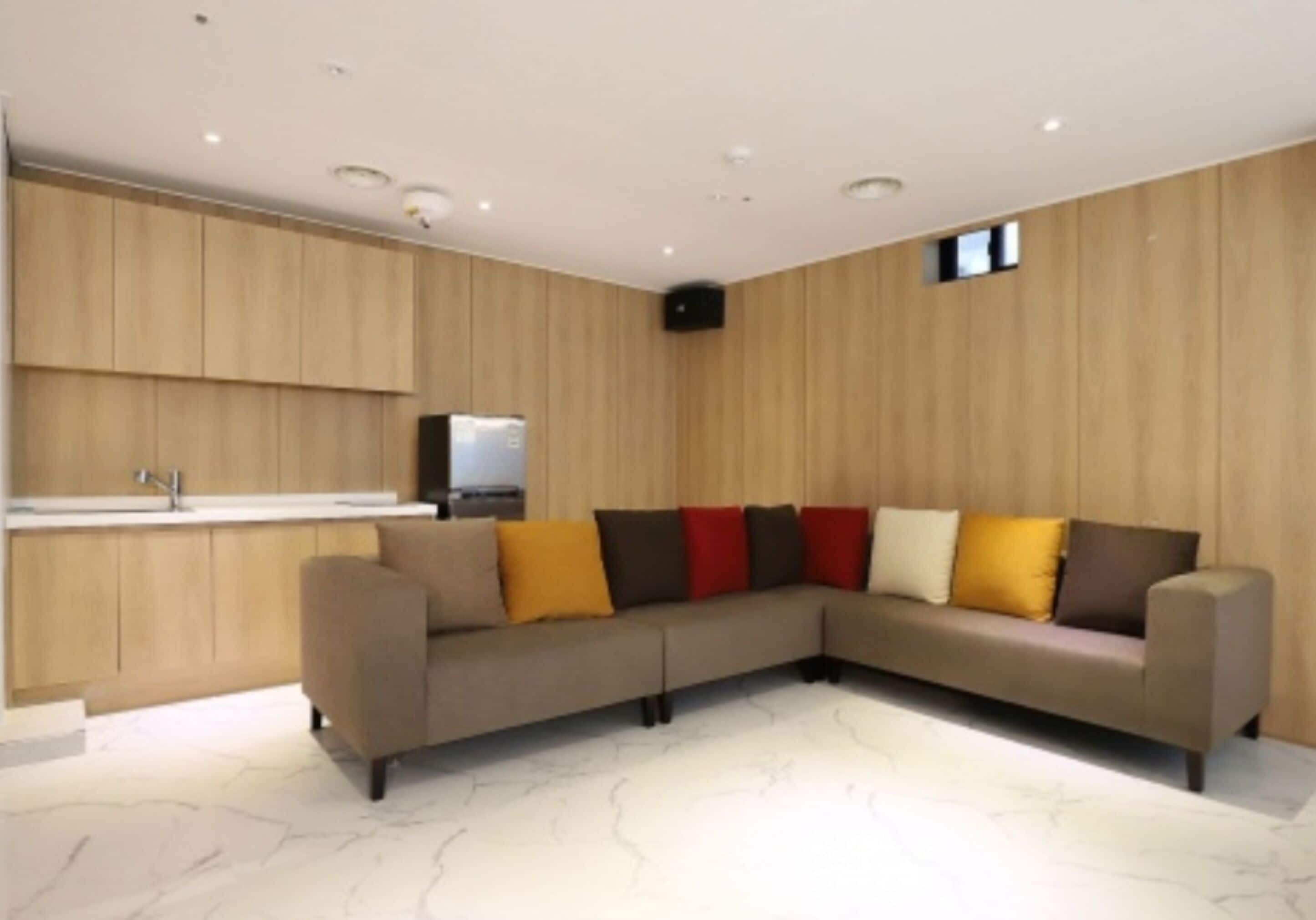 Uma sala de estar moderna com um sofá seccional bege, uma parede de madeira e uma cozinha com bancada branca.