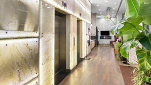 Um lobby limpo e moderno, com um balcão de recepção de mármore, elevadores e plantas em vasos.