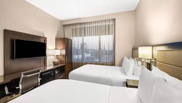 Quarto de hotel com uma cama grande, televisão presa na parede, escrivaninha com luminária e janela com cortinas.