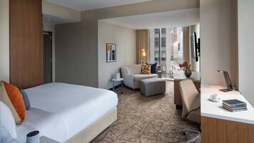 Quarto de hotel com uma cama grande, uma escrivaninha, uma cadeira e um sofá.