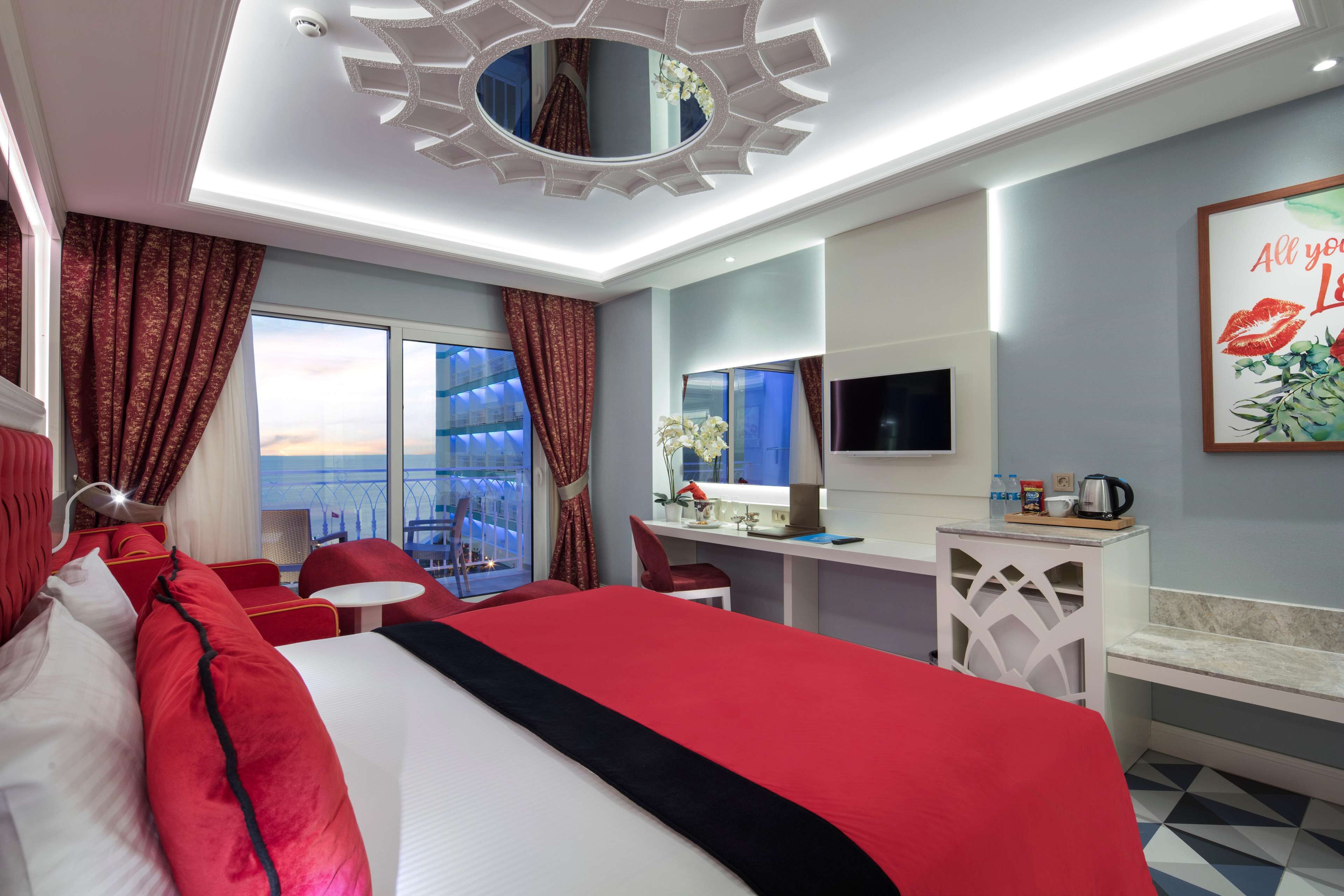 Quarto de hotel com uma cama grande, uma escrivaninha com computador, televisão e vista para a cidade.