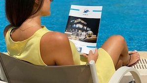 Uma pessoa sentada à beira da piscina com um folheto.