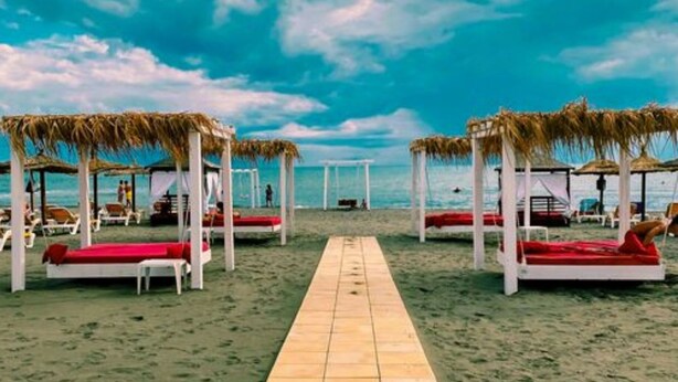 Uma praia com um calçadão de azulejos que leva a guarda-sóis e espreguiçadeiras.