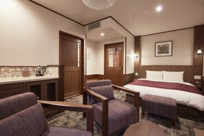 Quarto de hotel com uma cama, uma escrivaninha com chaleira, duas poltronas e uma pequena mesa.