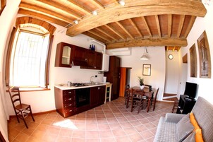 Cozinha com armários de madeira, sala de jantar com mesa e cadeiras, e sala de estar com sofá.