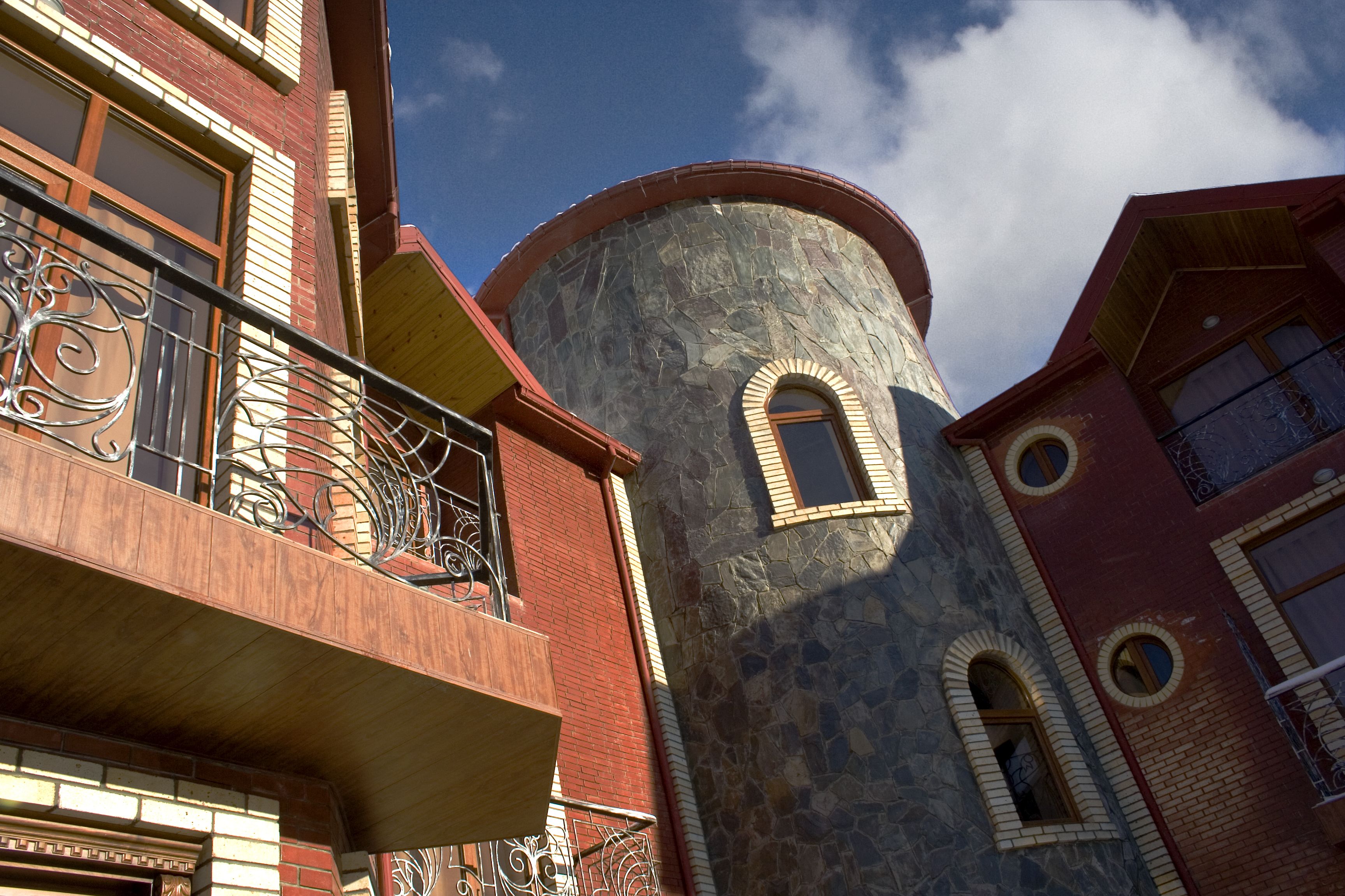 Um edifício de vários andares com uma torre de pedra, varandas com grades de ferro forjado e janelas em arco.