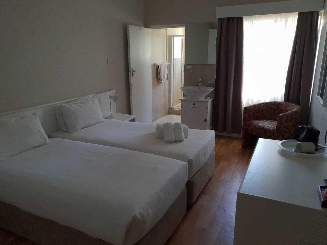 Quarto de hotel com duas camas, uma secretária pequena, uma cadeira, casa de banho e janela com cortinas.