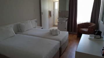 Quarto de hotel com duas camas, uma secretária pequena, uma cadeira, casa de banho e janela com cortinas.