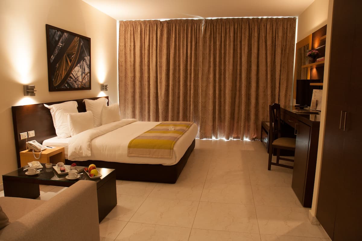 Quarto de hotel com cama, mesa de cabeceira, luminária e escrivaninha com cadeira.