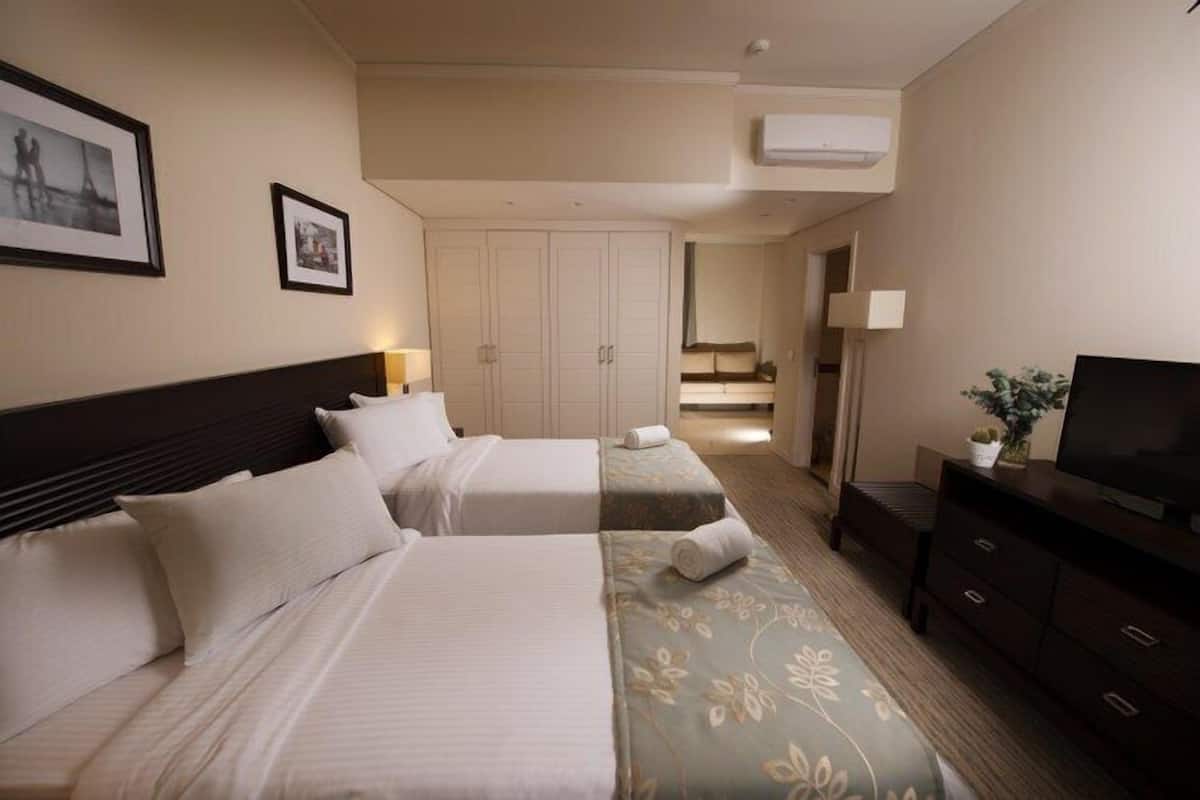 Quarto de hotel com duas camas, televisão, penteadeira e escada para um andar superior.