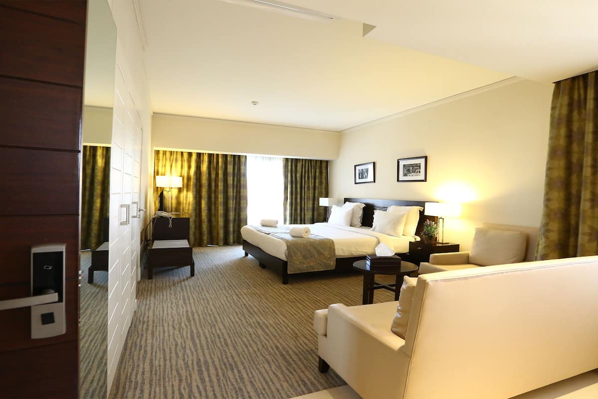 Quarto de hotel com cama, sofá, escrivaninha e luminária.