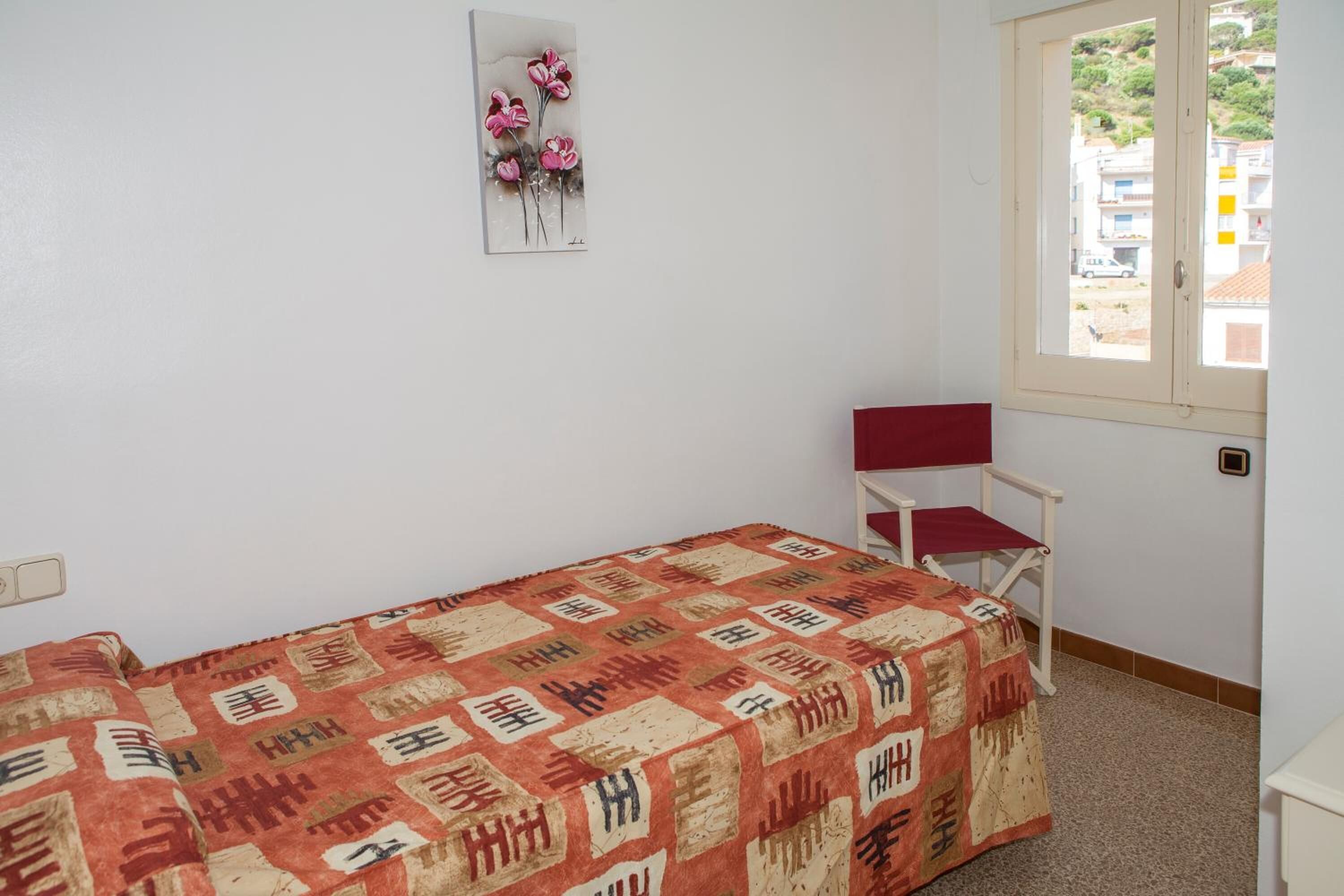 Um quarto pequeno com uma cama de solteiro, uma cadeira e uma janela.