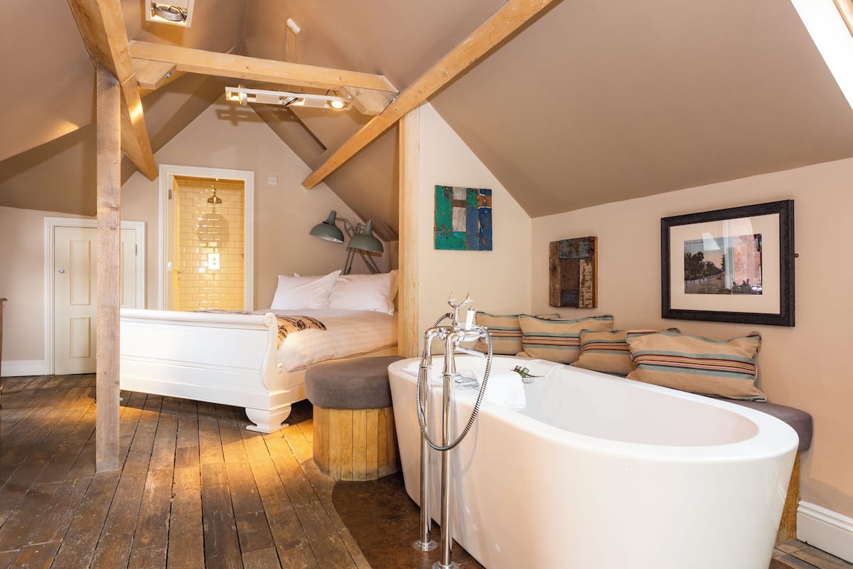 Quarto com uma cama grande, teto de madeira, banheira e porta que dá para outro espaço.