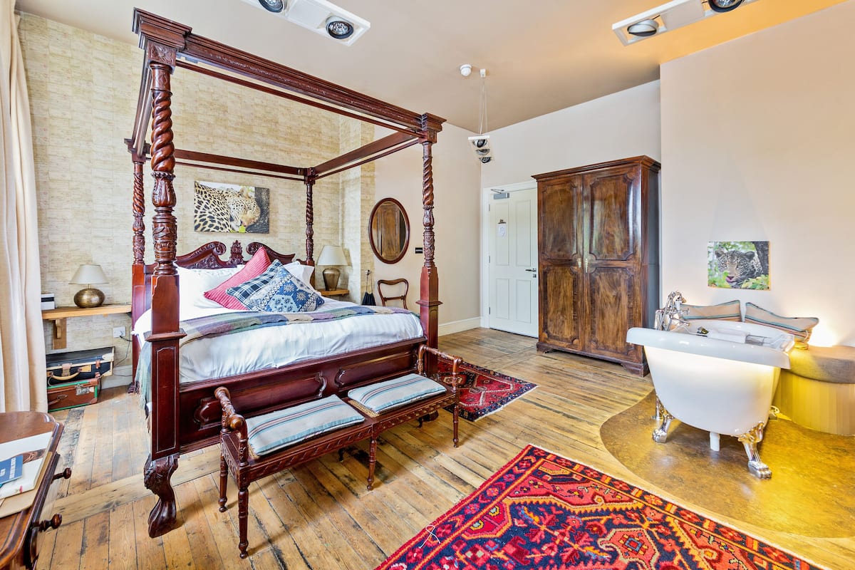 Um quarto espaçoso com cama de dossel, banheira de patas de leão e um espelho grande.