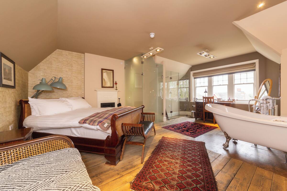 Quarto com cama grande, área de estar, banheiro com banheira e lareira.