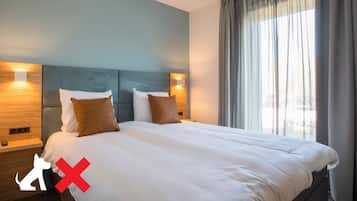 Quarto de hotel com cama grande, duas mesas de cabeceira e uma janela com cortinas.