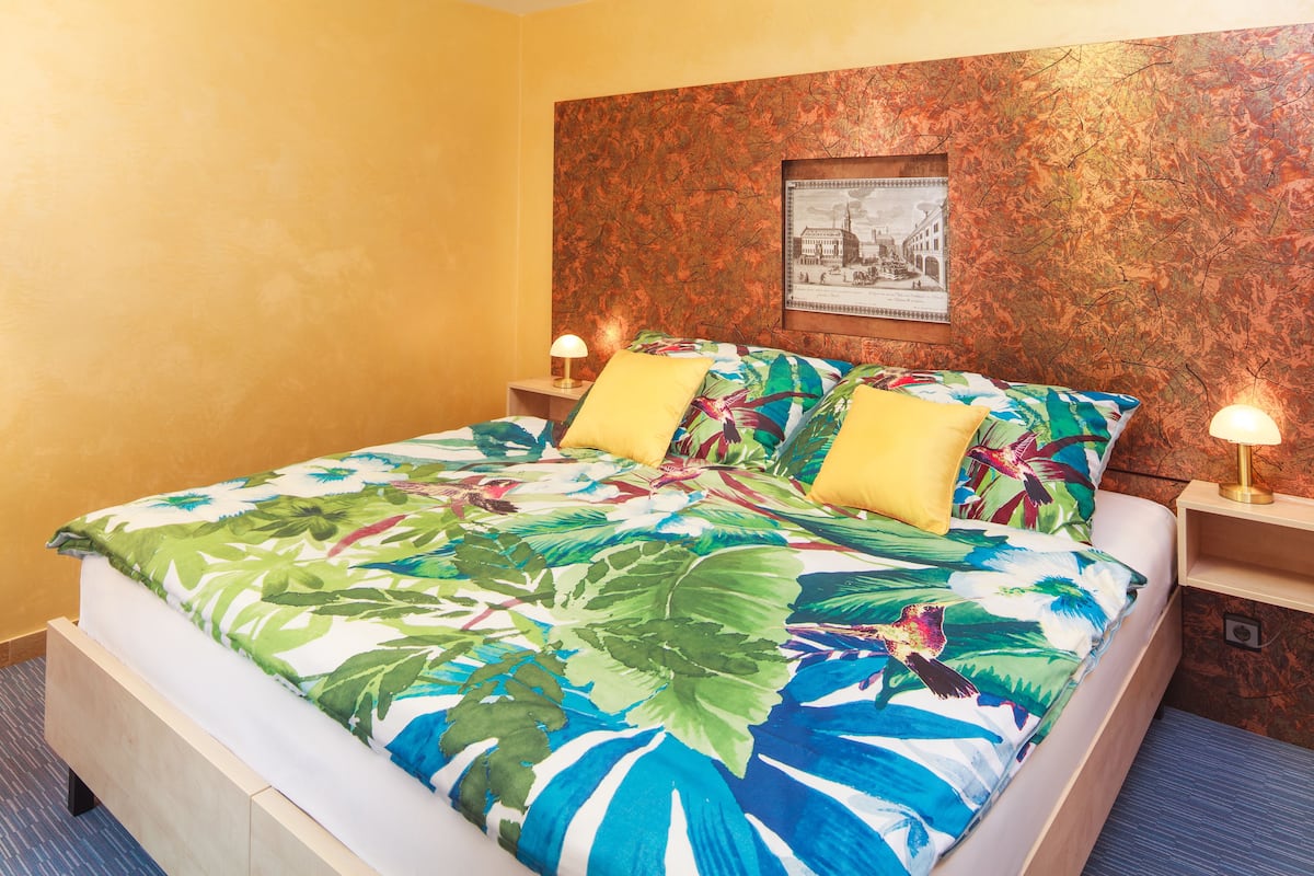 Cama com colcha florida, dois travesseiros amarelos e duas luminárias de cabeceira.